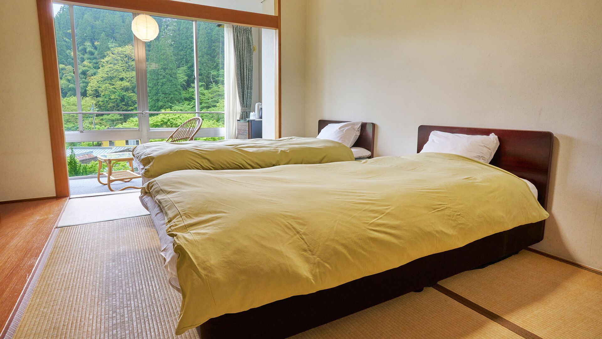 Quarto com duas camas, vista para o verde lá fora e uma cadeira junto à janela.