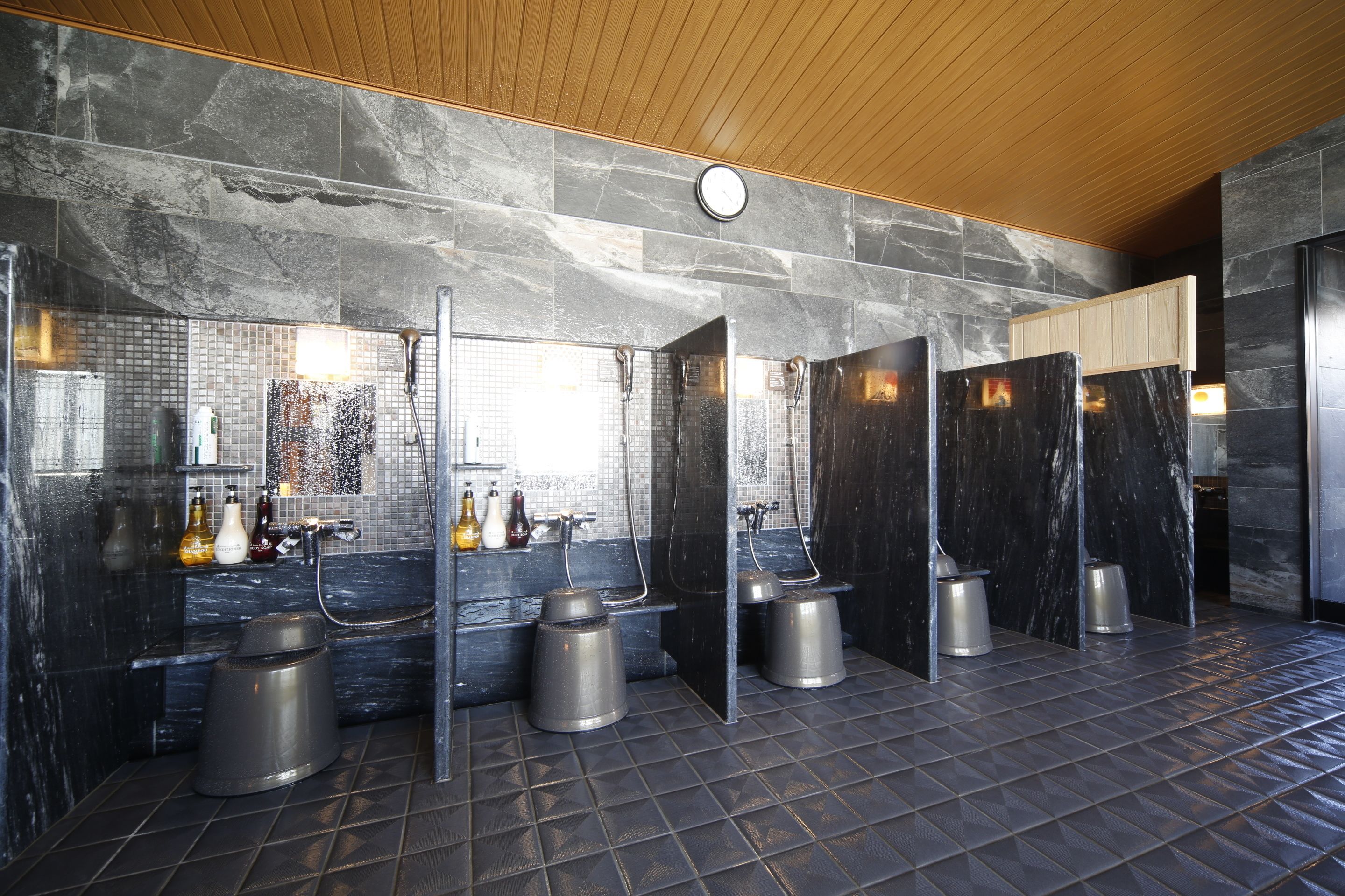 Casa de banho moderna com paredes de mármore, teto de madeira e várias pias com cestos de metal.