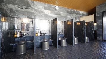 Casa de banho moderna com paredes de mármore, teto de madeira e várias pias com cestos de metal.