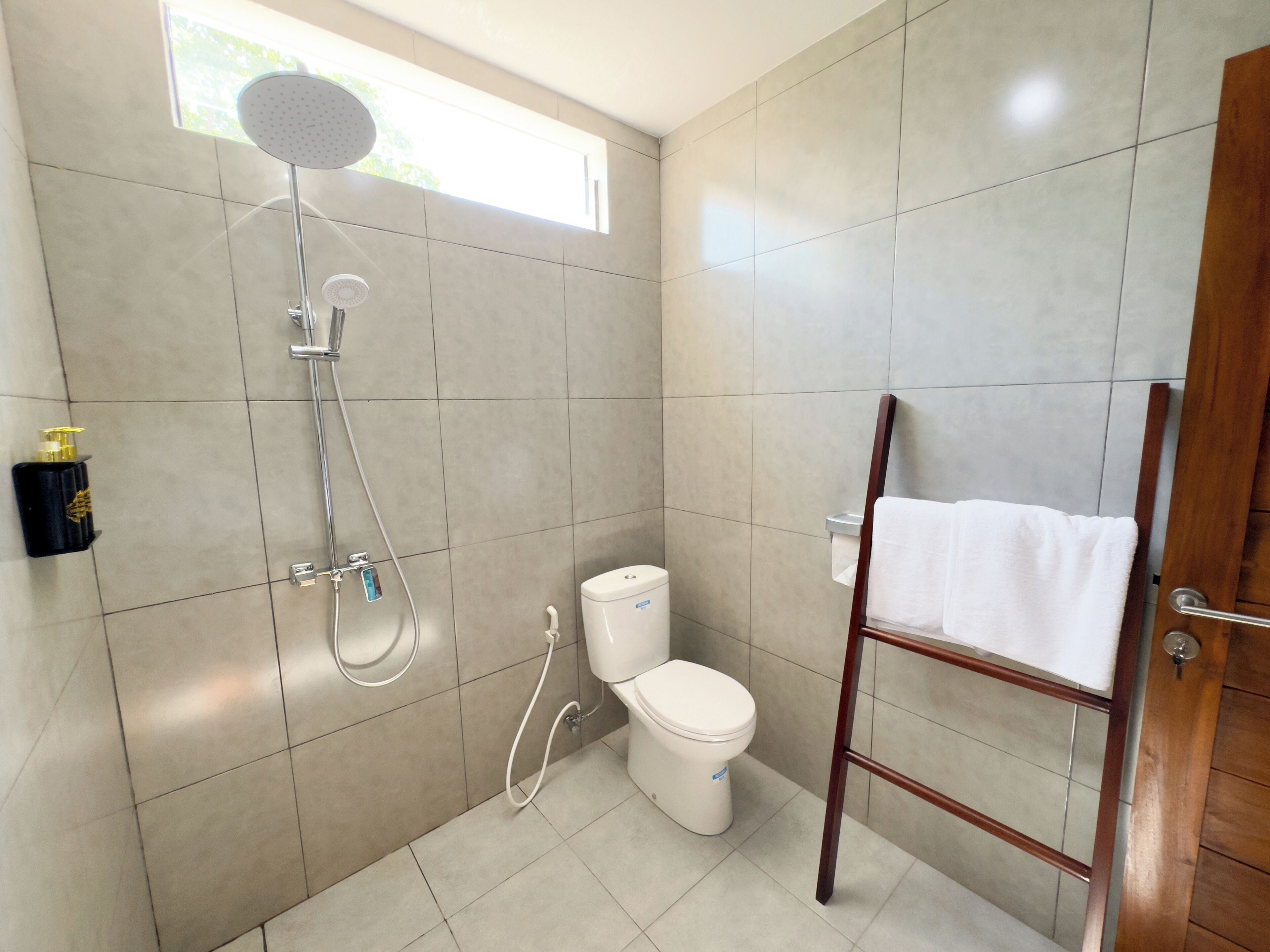Uma casa de banho moderna com chuveiro, sanita e um porta-toalhas de madeira.