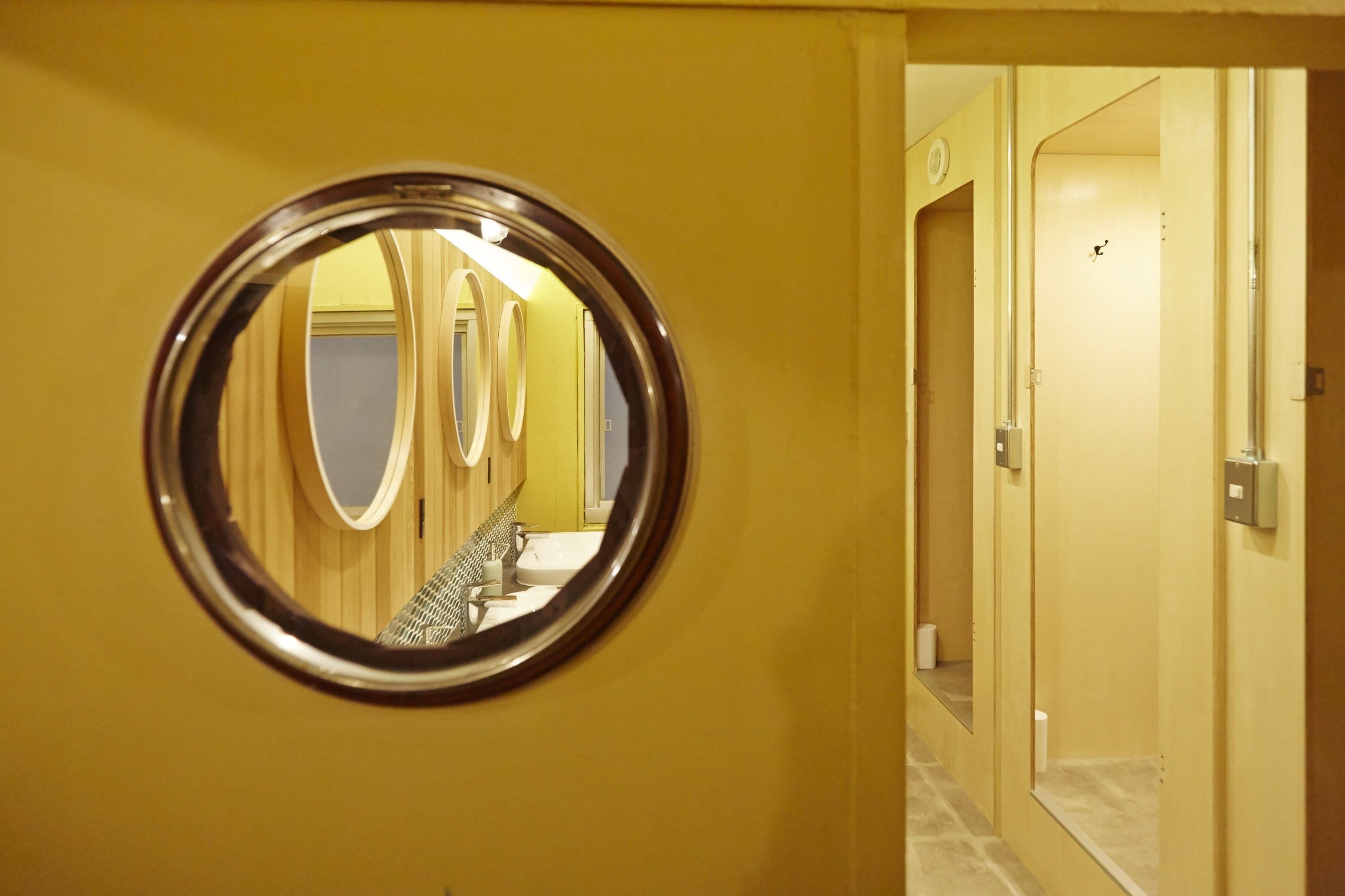 Corredor com um espelho redondo refletindo um banheiro com pia e porta-toalhas.