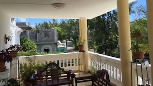 Varanda com banco de madeira, plantas em vasos e vista para um edifício e árvores.