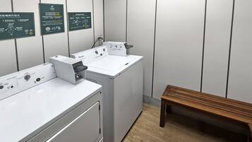 Uma lavanderia com duas secadoras Whirlpool e um banco de madeira. Instruções para usar as secadoras estão afixadas na parede.