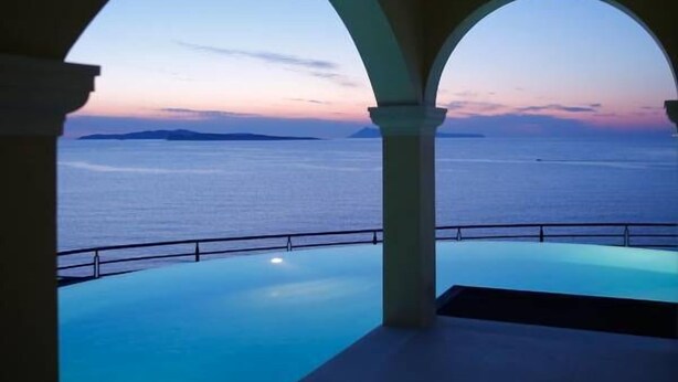 Vista de uma piscina infinita com o mar e o pôr do sol.