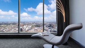 Quarto de hotel moderno com uma grande janela que oferece vista para a cidade, uma cadeira contemporânea e uma revista no peitoril.