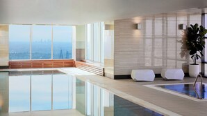 Piscina interna moderna com vista para a cidade, um banco de madeira e um vaso de planta.