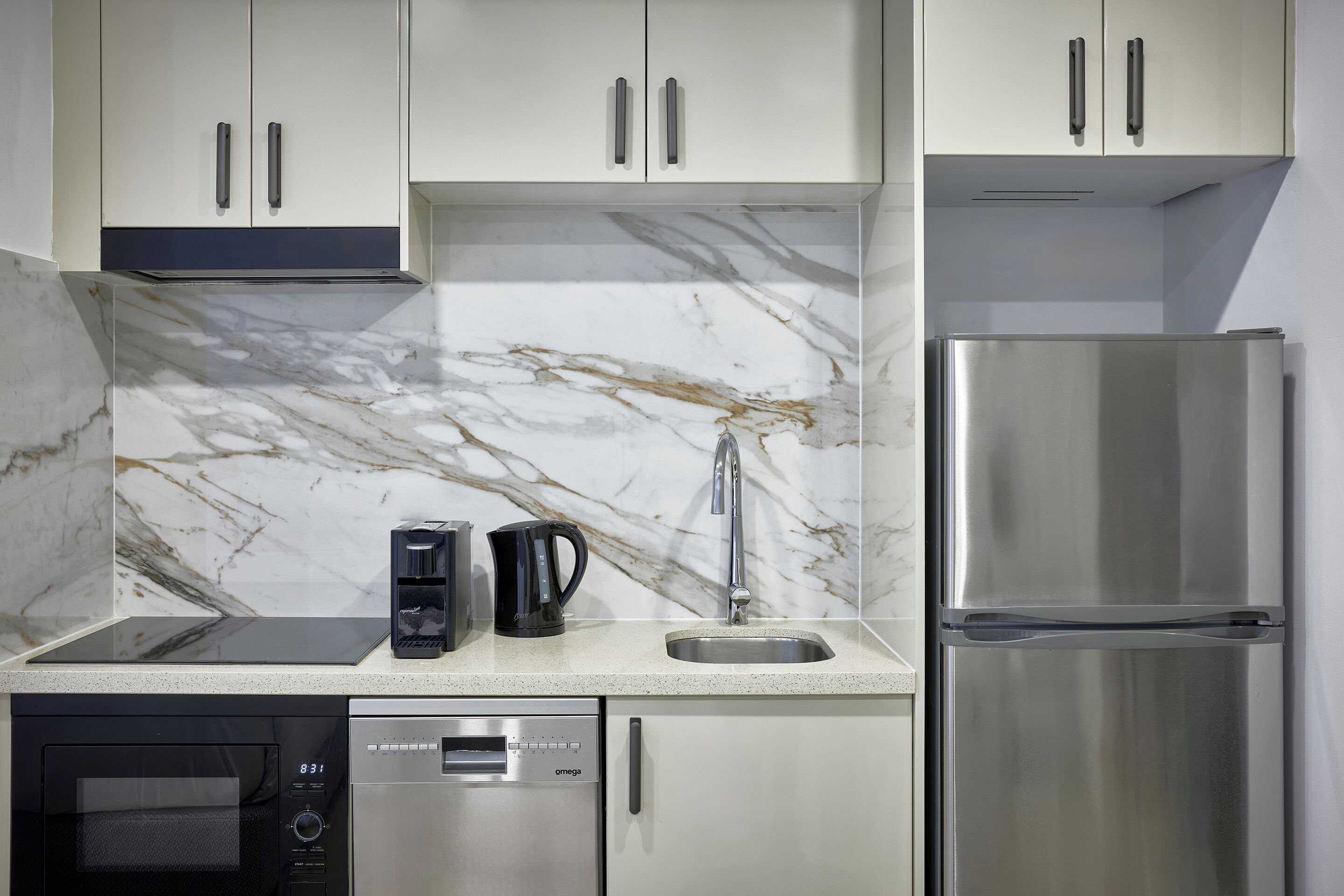 Uma cozinha moderna com armários brancos, painel de proteção de mármore, geladeira de aço inoxidável, lava-louças e máquina de café.