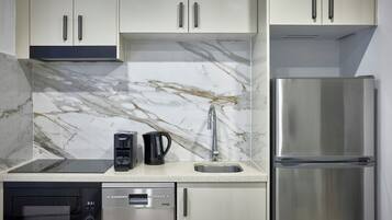 Uma cozinha moderna com armários brancos, painel de proteção de mármore, geladeira de aço inoxidável, lava-louças e máquina de café.