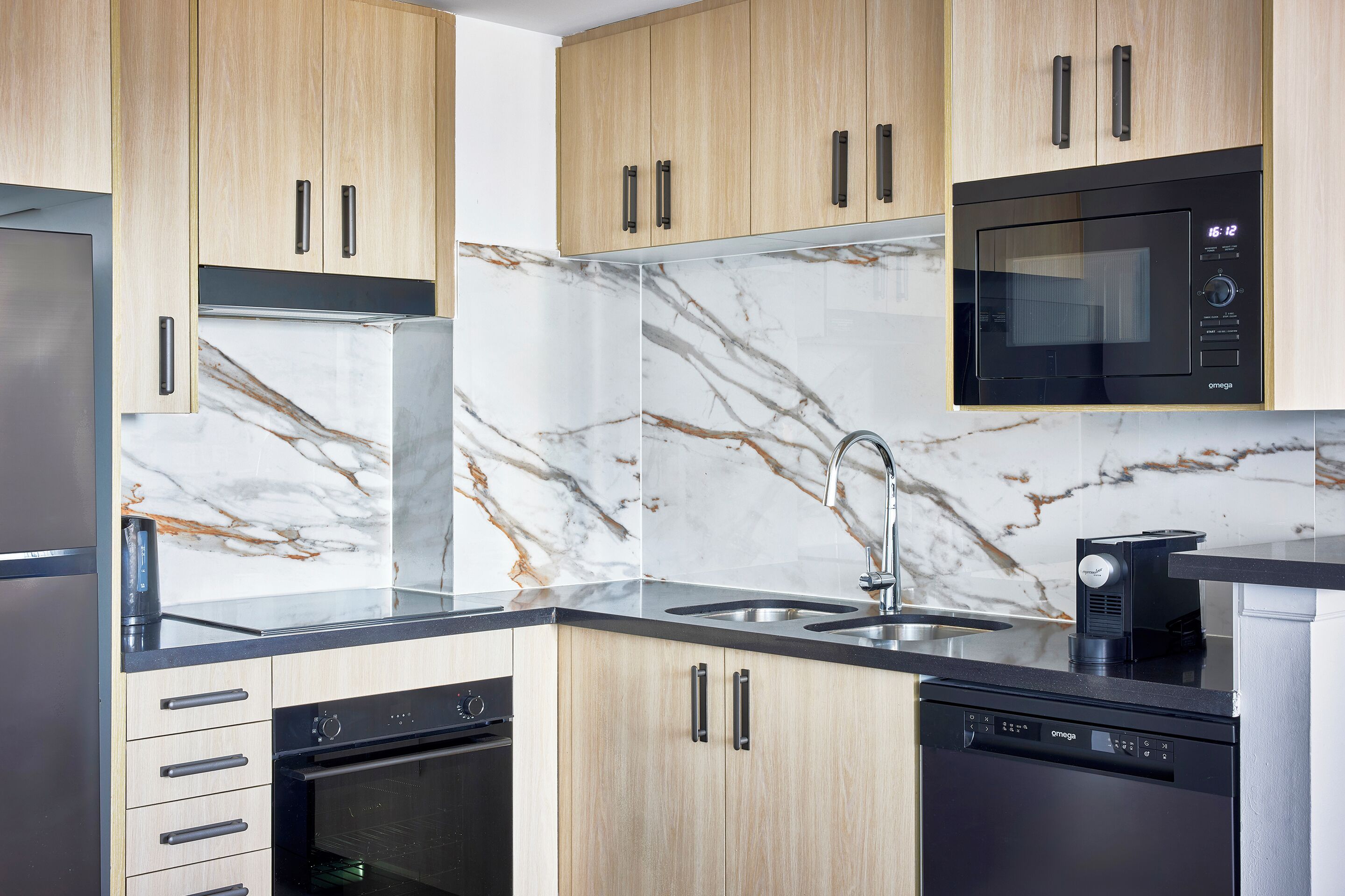 Uma cozinha com armários de madeira, micro-ondas embutido, lava-louças e painel de fundo em mármore.