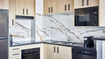 Uma cozinha com armários de madeira, micro-ondas embutido, lava-louças e painel de fundo em mármore.