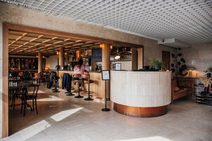 Uma área de bar com balcão, banquetas e um espaço de estar com mesas e cadeiras.