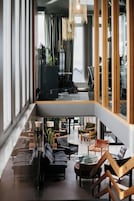 Um lobby moderno de hotel com um mezanino, áreas de estar e vista para a rua.