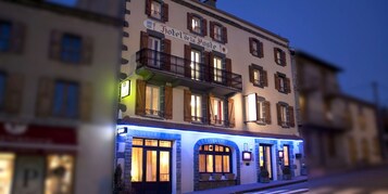 Um hotel com uma placa que diz "Hotel della Poste". Apresenta várias varandas com grades de madeira e detalhes em pedra.