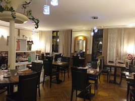 Restaurante com várias mesas e cadeiras, piso de madeira e luminárias pendentes.