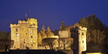 Um castelo medieval com uma torre central, uma torre redonda menor e uma muralha fortificada.
