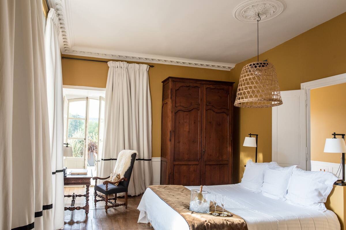 Quarto com cama, guarda-roupa de madeira, cadeira e janela com cortinas.