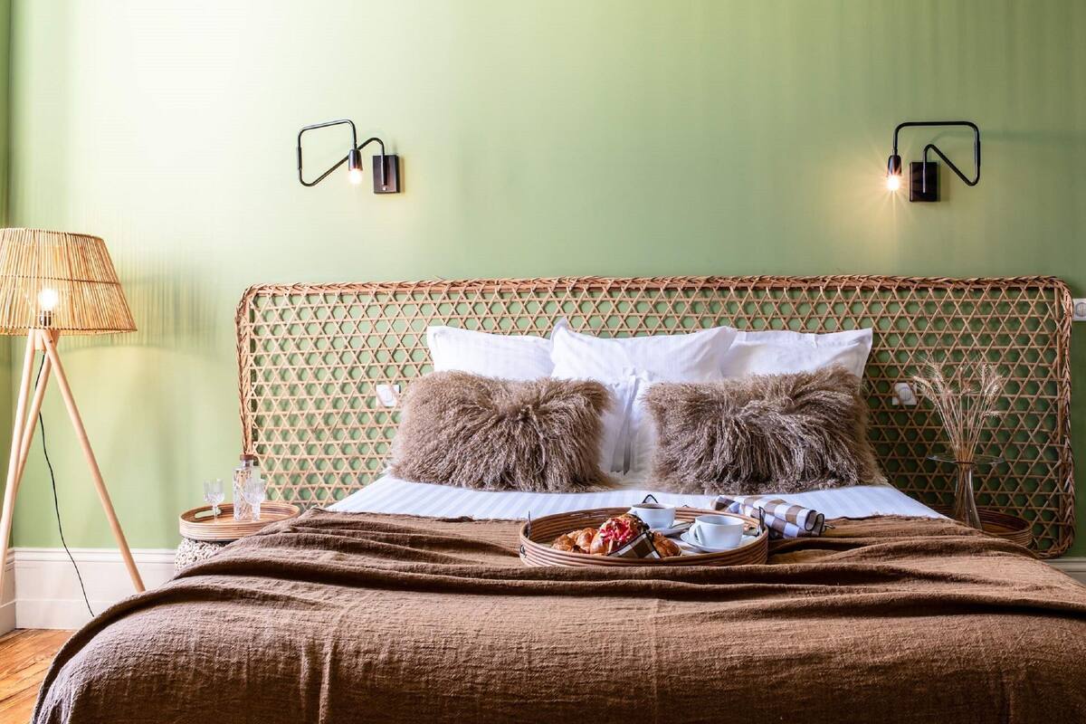 Cama bem arrumada com cabeceira de tear, luminária de cabeceira e bandeja com itens de café da manhã.