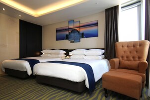 Quarto de hotel com uma cama grande, uma poltrona marrom e uma pintura de um pôr do sol na parede.