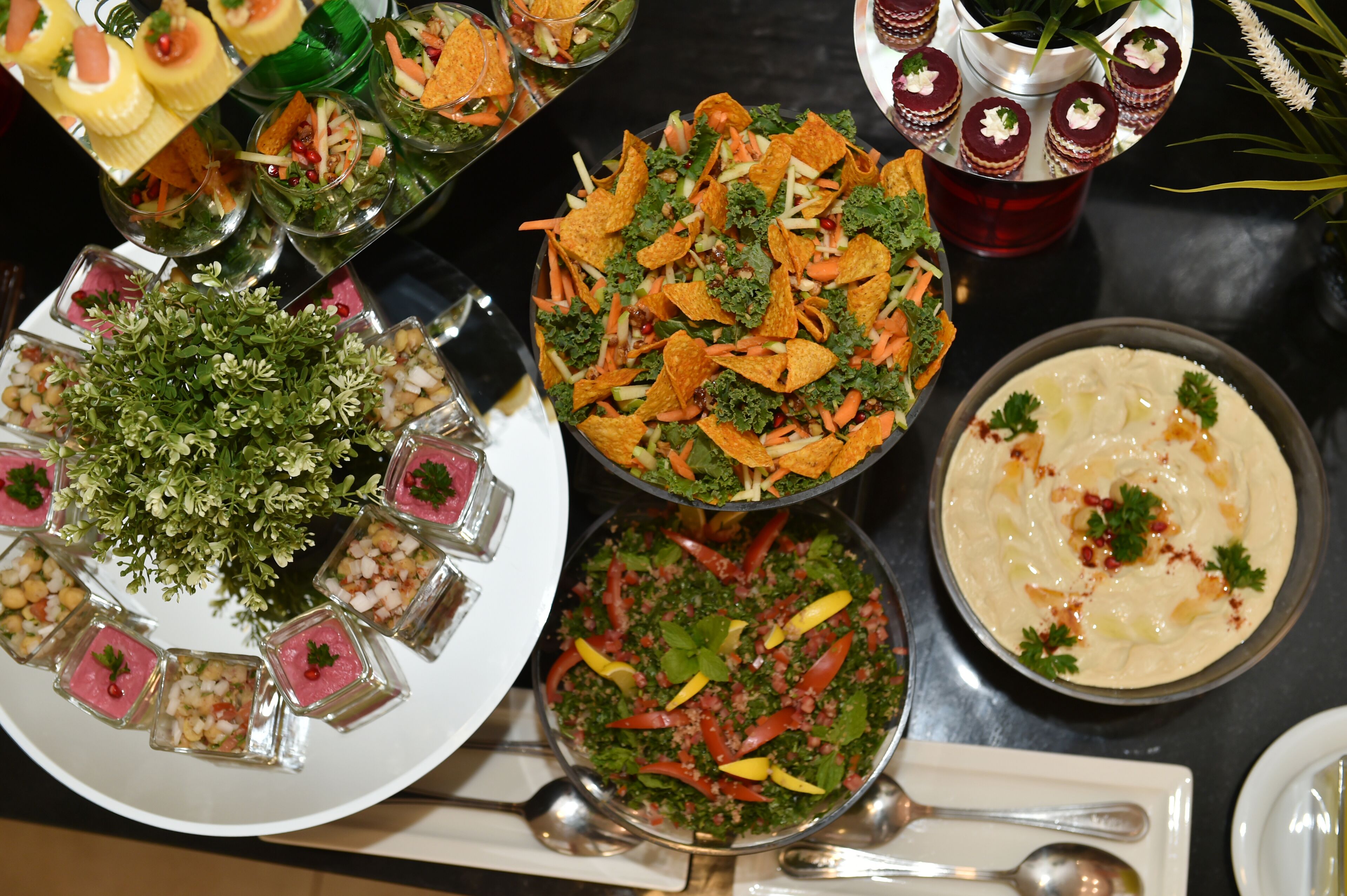 Diversos pratos, incluindo uma salada com vegetais desfiados, uma tigela de molho cremoso decorada com ervas, e vários pequenos recipientes de vidro com diferentes alimentos.