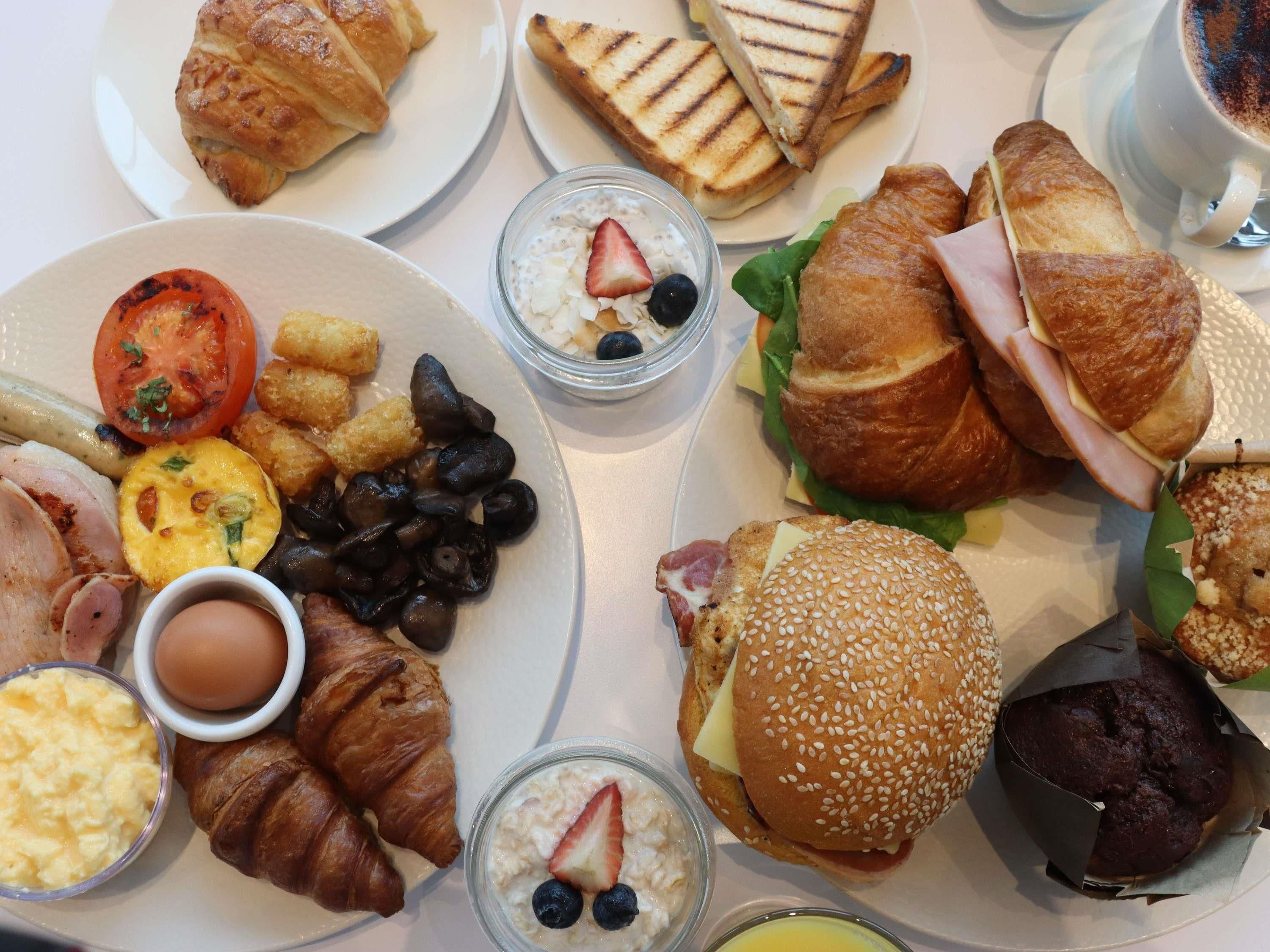 Um buffet de café da manhã com diversas opções de comida, incluindo croissants, sanduíches grelhados, ovos e frutas.