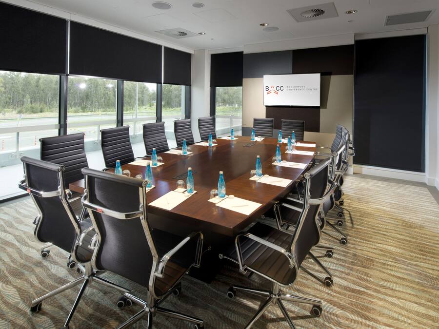 Uma sala de conferências com uma mesa grande, cadeiras, garrafas de água e uma tela de apresentação.