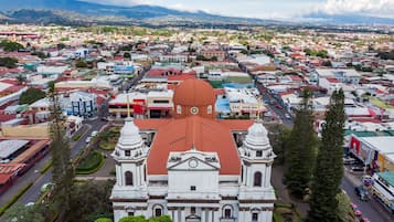 Um edifício grande e branco com telhado vermelho e duas cúpulas, rodeado por uma paisagem urbana com vários edifícios e vegetação.
