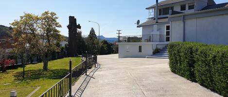 Uma rua residencial com uma casa moderna, um caminho de concreto e uma árvore grande.
