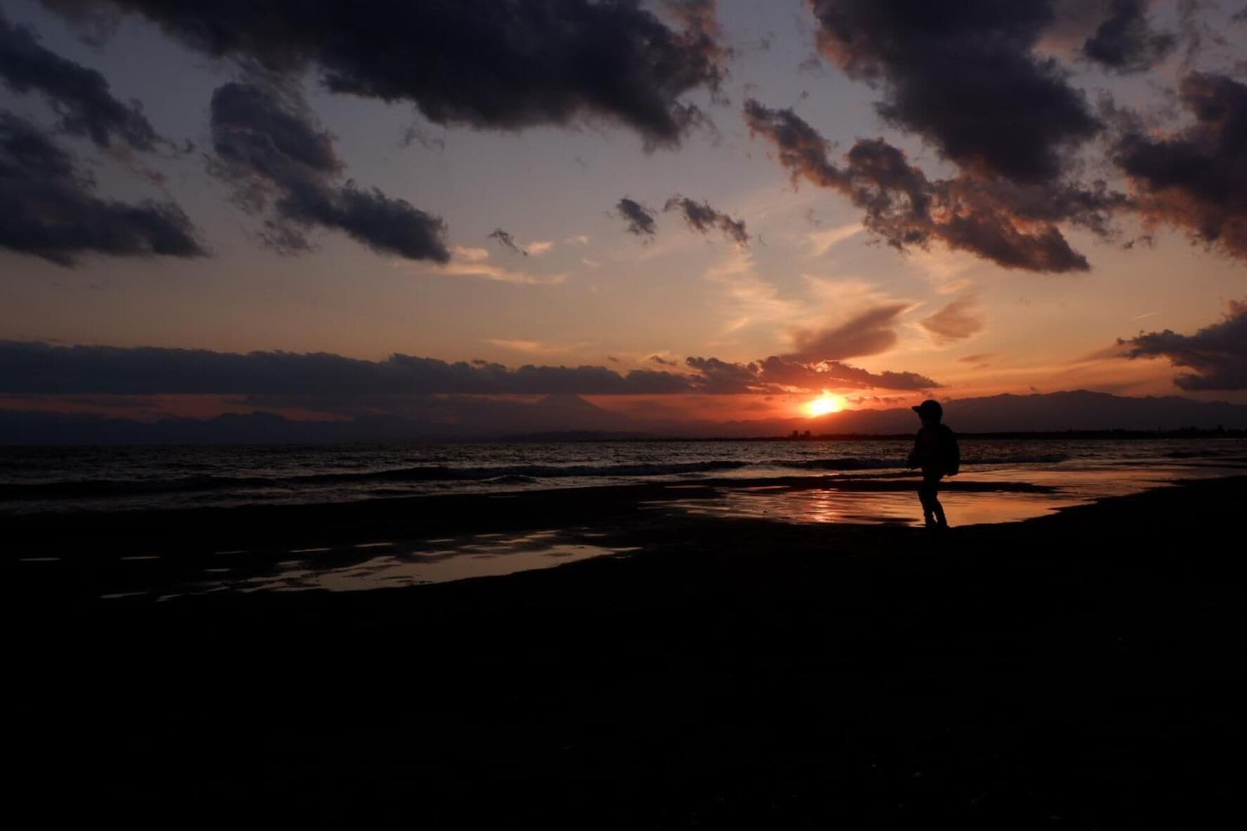 Cena de praia com uma pessoa silhuetada contra o pôr do sol.