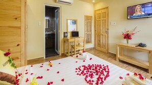 Quarto de hotel com cama, escrivaninha, televisão e banheiro visível através de uma porta aberta.