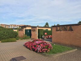 Entrada de hotel com fachada de tijolos, um portão verde e um canteiro de flores cor-de-rosa.