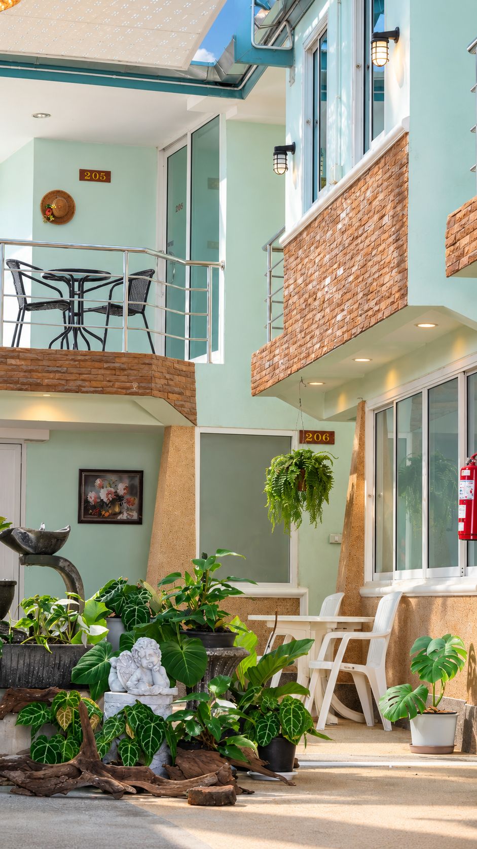 Hotel com varanda, área de estar externa e diversos vasos de plantas.