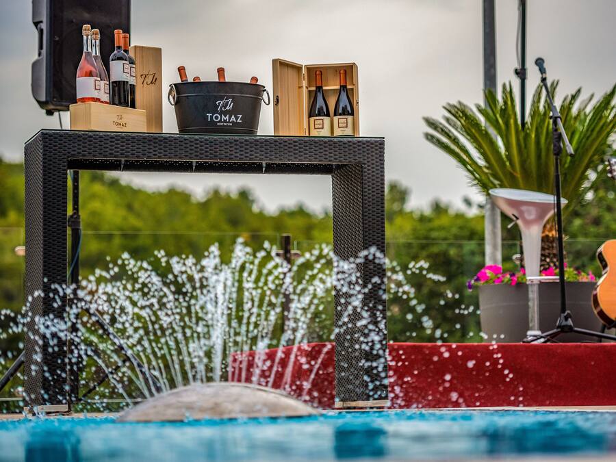 Cenário à beira da piscina com mesa, garrafas e um violão.