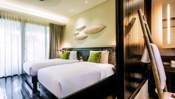 Quarto de hotel com duas camas, uma janela grande com cortinas, um objeto decorativo na parede e um porta-toalhas de madeira.