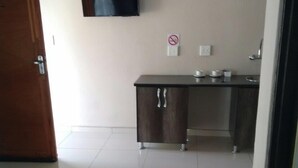 Um quarto com cama, porta de madeira, cozinha compacta com pia e televisão fixada na parede.