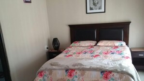 Quarto com cama, mesa de cabeceira, quadro na parede e relógio.
