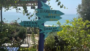 Um sinal de direção com várias setas indicando diferentes destinos, incluindo Miami, Biarritz, Londres, Ocean Blues Cafe e Banana Beach.