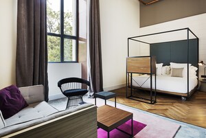 Quarto moderno com sofá, poltrona, mesa pequena e cama com dossel.