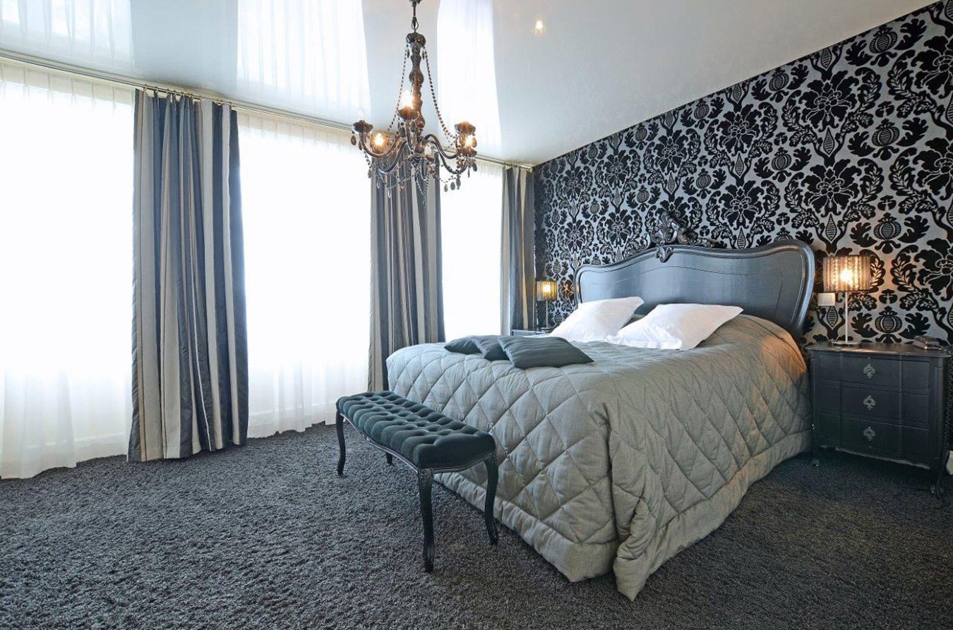 Quarto com uma cama grande, um banquinho, um candelabro e parede estampada.