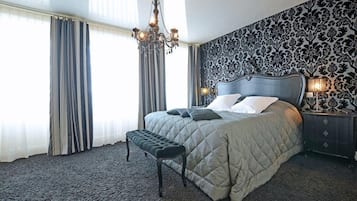 Quarto com uma cama grande, um banquinho, um candelabro e parede estampada.