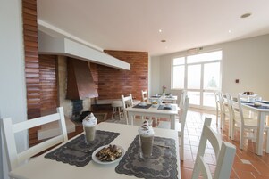 Uma sala de jantar com móveis brancos, parede de tijolos e uma grande janela.