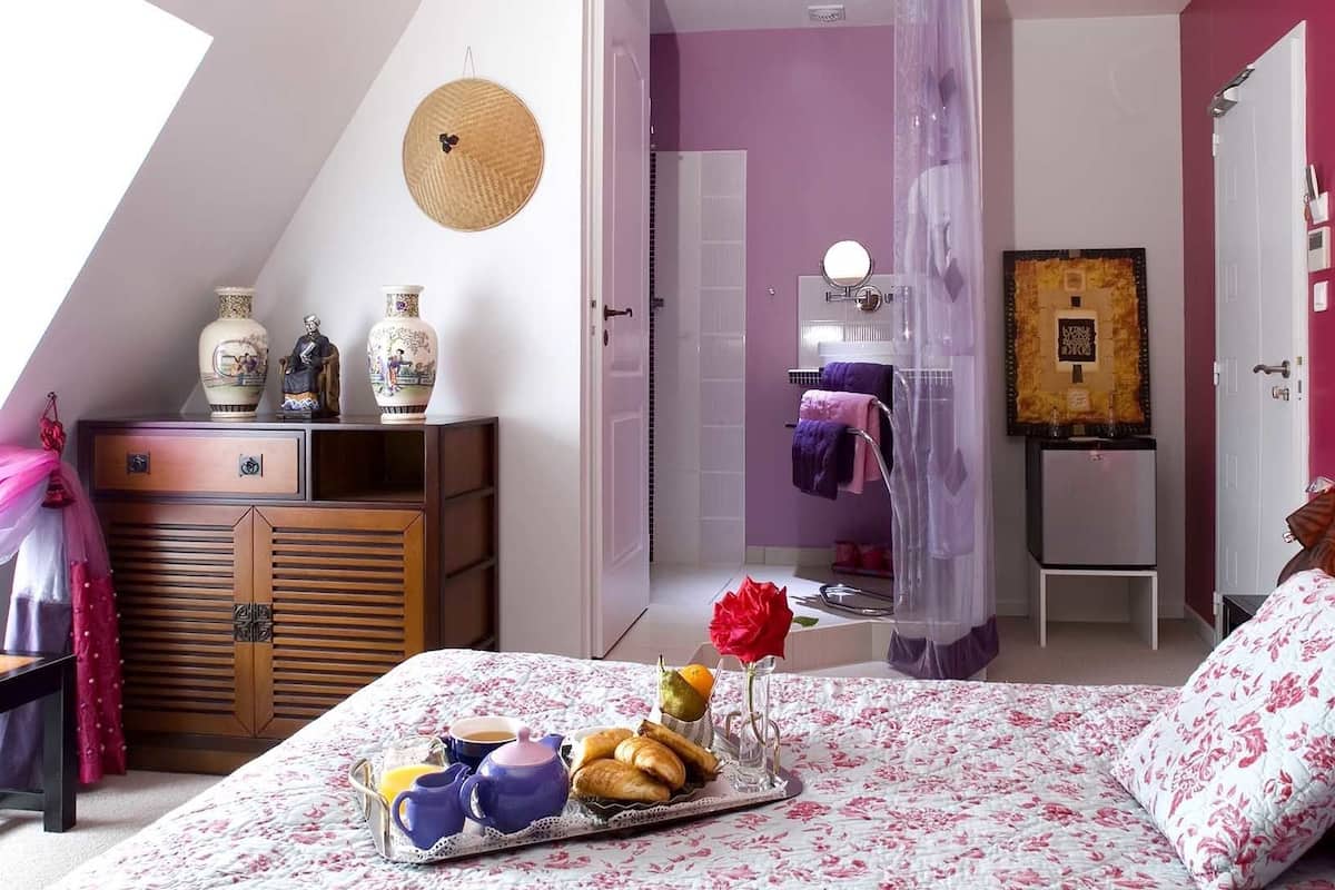Quarto com cama, cômoda, penteadeira e banheiro visível por uma porta aberta.