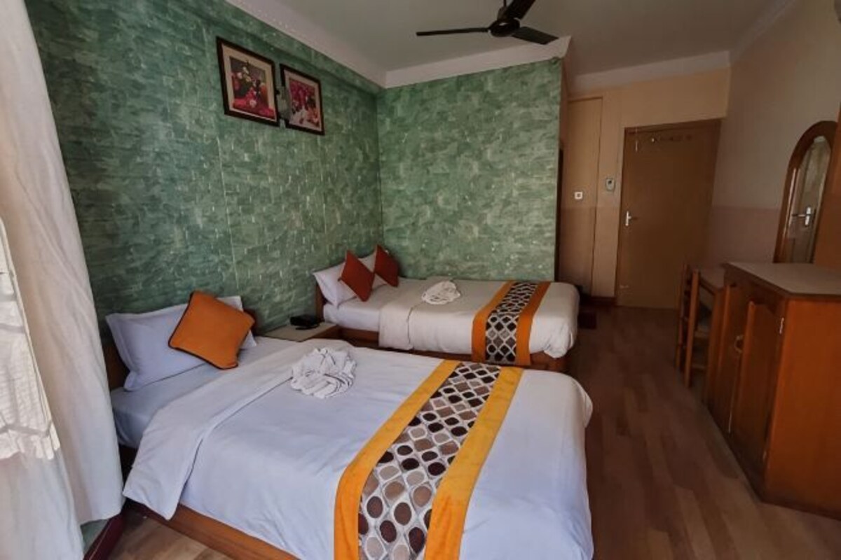 Quarto de hotel com duas camas, um guarda-roupa de madeira e um ventilador de teto.