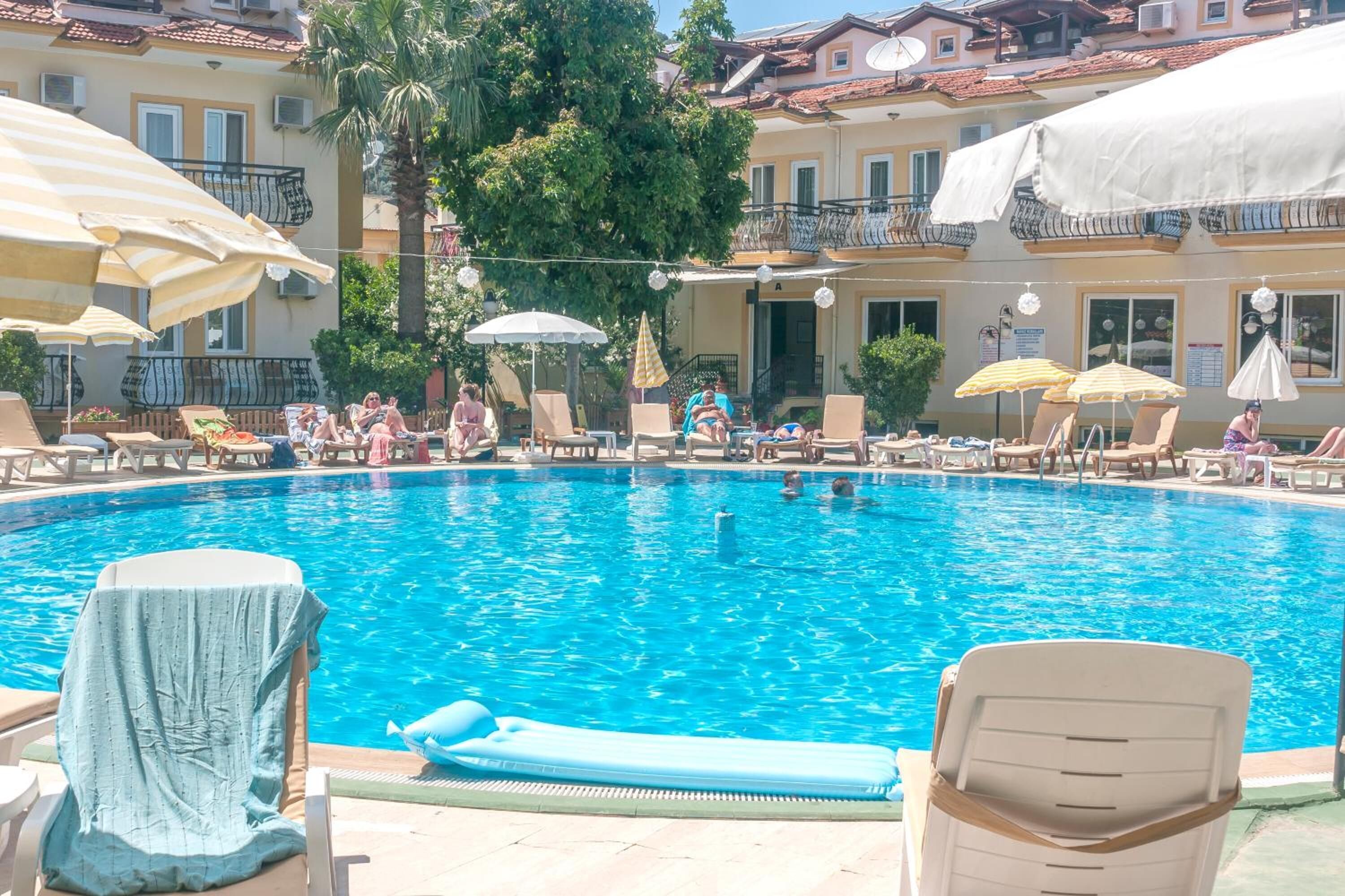 Uma piscina com espreguiçadeiras e guarda-sóis, cercada por edifícios com varandas.