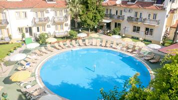 Uma piscina circular com espreguiçadeiras e guarda-sóis, rodeada por um edifício com varandas e um jardim.