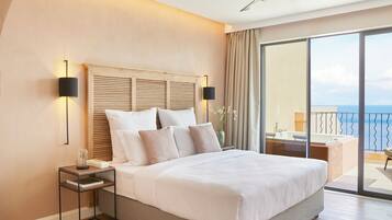 Quarto de hotel moderno com uma cama grande, um ventilador de teto, uma mesa de cabeceira e vista para o mar através de uma varanda.