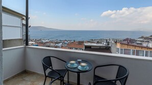 Varanda com duas cadeiras e uma mesa, com vista para a costa, edifícios e o mar.