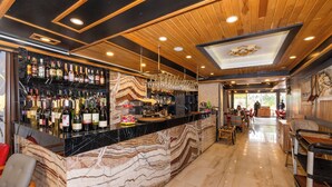 Uma área de bar com bancada de mármore, teto de madeira e diversos copos e garrafas.