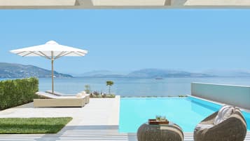 Área de piscina com espreguiçadeiras e um guarda-sol, com vista para um corpo d'água e montanhas ao longe.