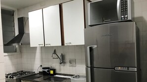 Cozinha com armários brancos, geladeira de aço inoxidável, micro-ondas, fogão a gás e pia.