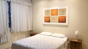 Quarto com cama, mesa de cabeceira, obra de arte na parede e janela com cortinas.
